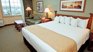 Quarto de hotel com uma cama grande, uma escrivaninha, uma cadeira, uma mesa de cabeceira e uma janela com vista para o exterior.