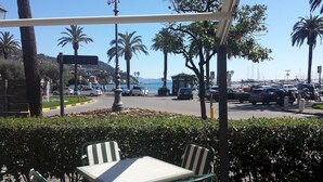 Uma rua costeira com carros estacionados, palmeiras e vista para o mar.