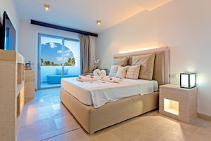 Quarto de hotel moderno com uma cama grande, uma mesinha de cabeceira com abajur e vista para o exterior.