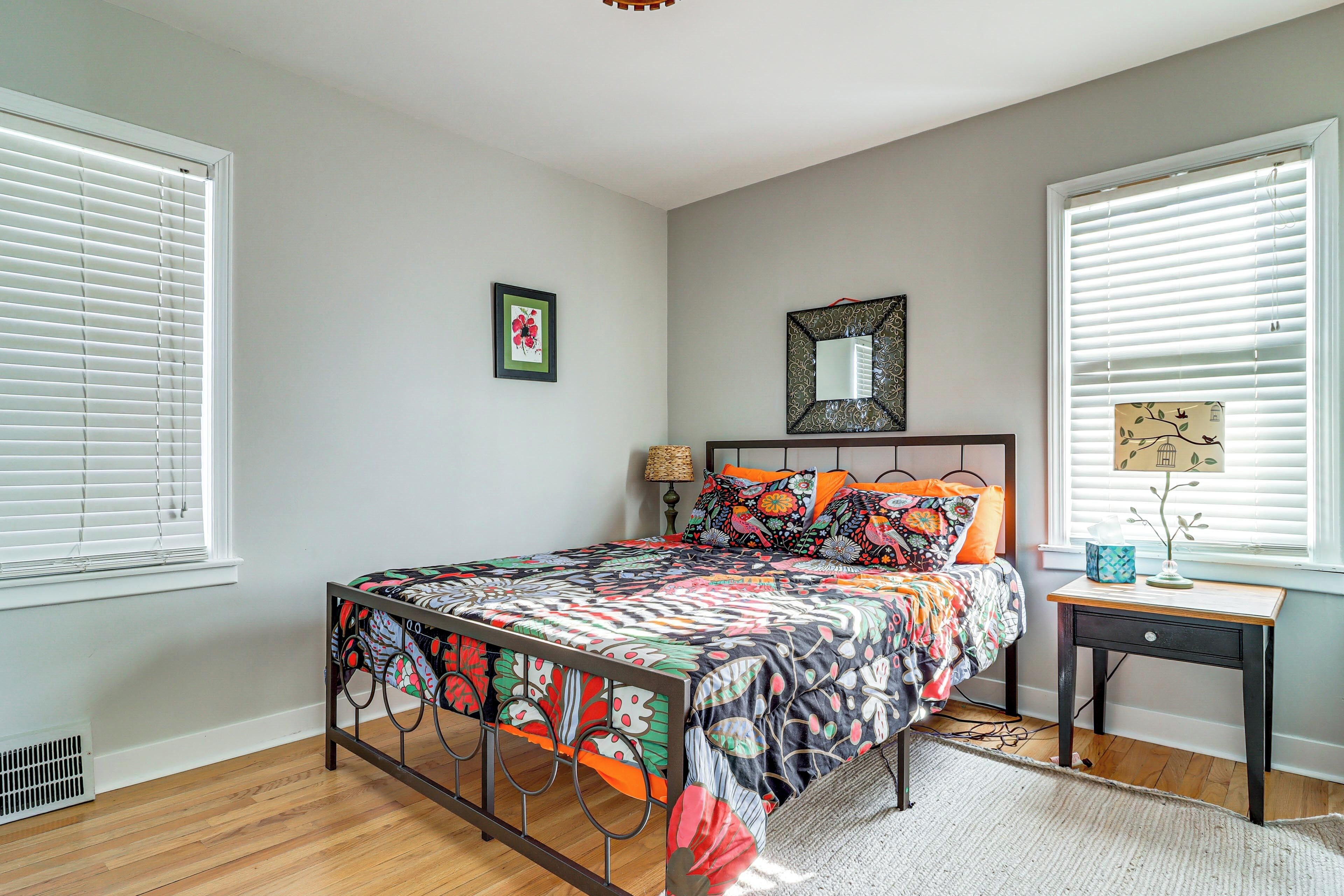 Quarto com cama, mesa de cabeceira, abajur e janela com persianas.