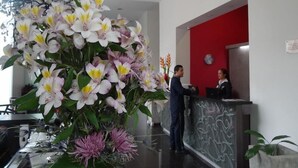 Uma área de recepção com um arranjo floral grande, um balcão de recepção e um relógio na parede.