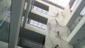 Um átrio de vários níveis com design arquitetônico moderno, com guarda-corpos de vidro e uma instalação artística original na parede.
