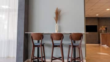 Uma área de bar com três banquetas de madeira, um vaso central com plantas secas e um design de interiores moderno.