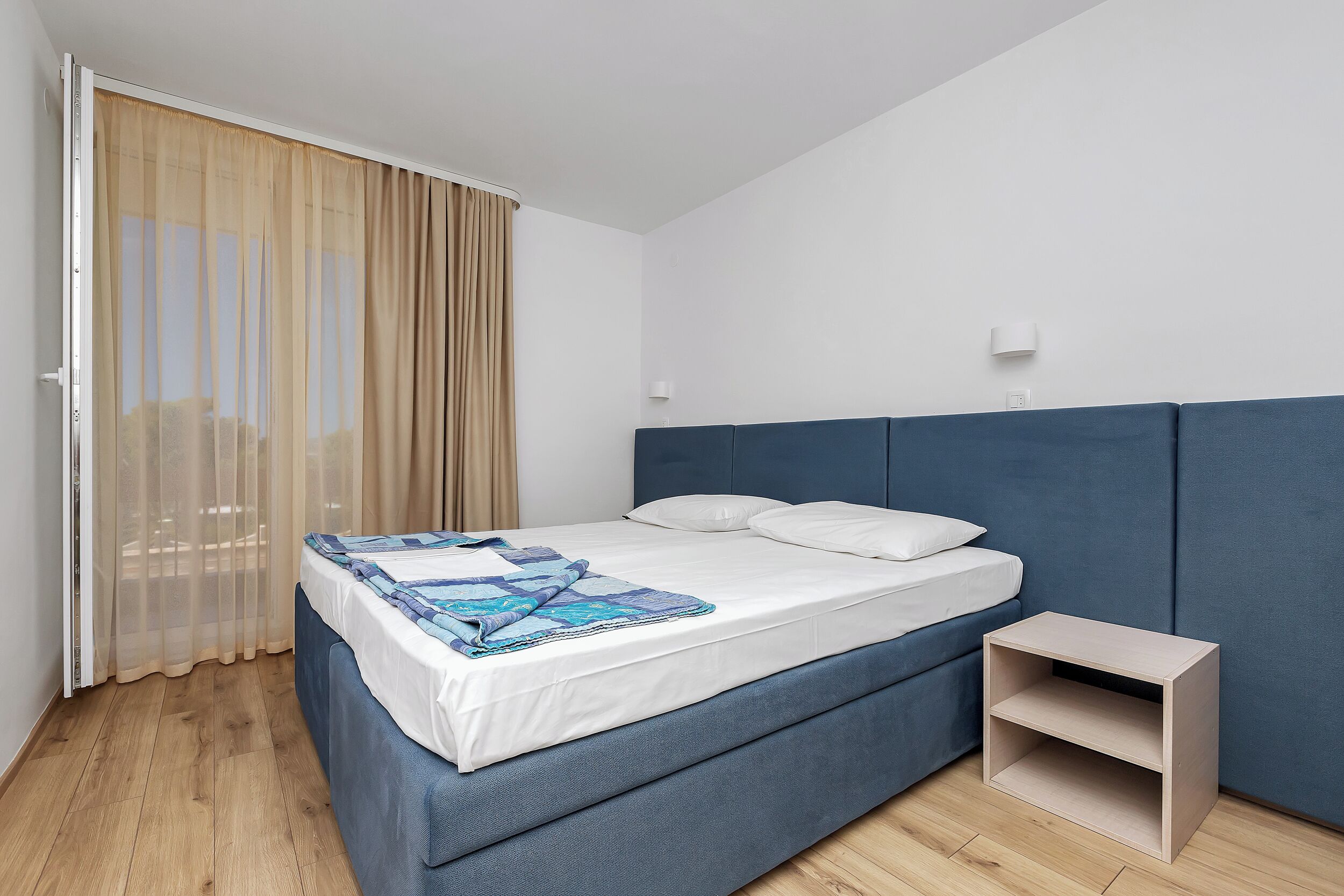 Quarto com cama, mesa de cabeceira e janela com cortinas.
