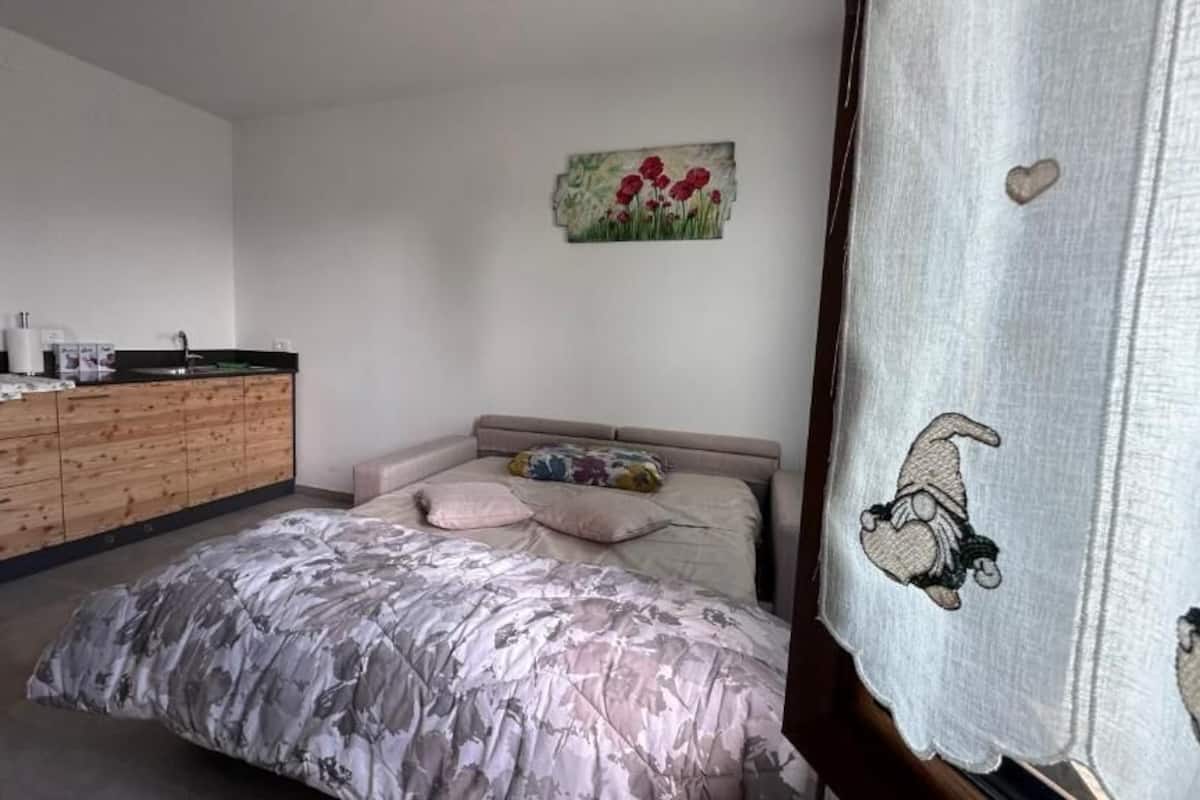 Quarto com cama, cómoda de madeira, pintura na parede e cortina com desenho de gnomo.