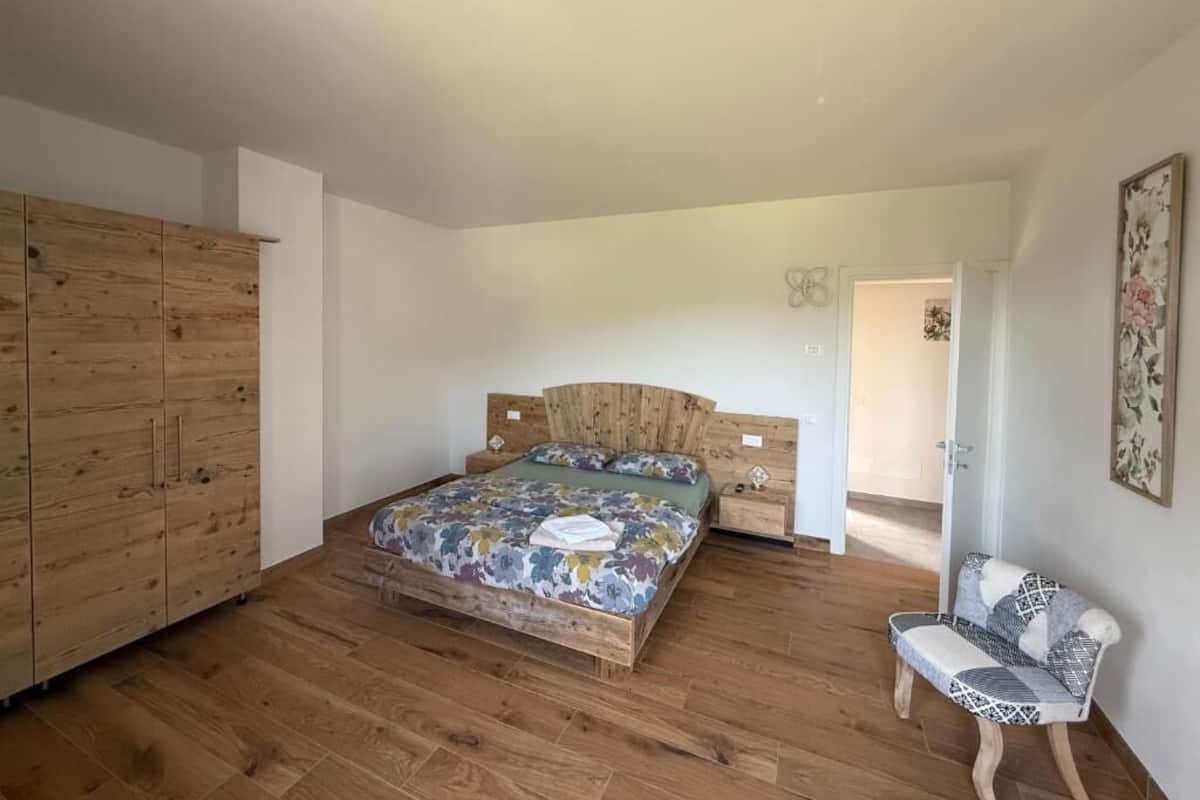 Quarto com cama de madeira, mesa de cabeceira, uma cadeira e guarda-roupa.
