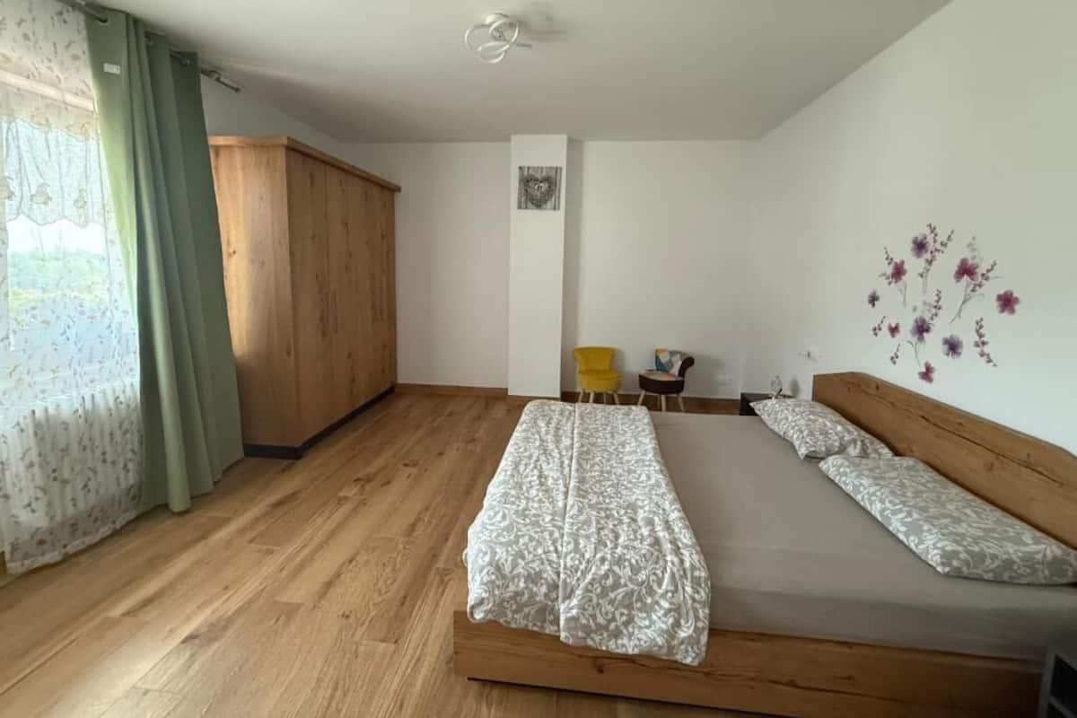 Quarto com cama de madeira, uma mesinha, uma cadeira e um guarda-roupa.