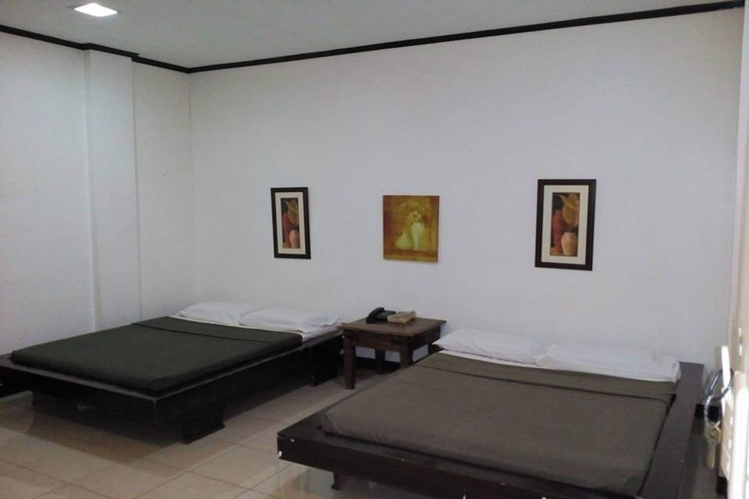 Quarto com duas camas de solteiro, uma pequena mesa e três quadros na parede.