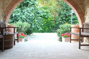 Uma área de jardim ao ar livre com arcos de tijolo, bancos de madeira e plantas em vasos.