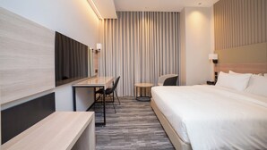 Quarto de hotel moderno com cama, escrivaninha, cadeira e um espelho grande.