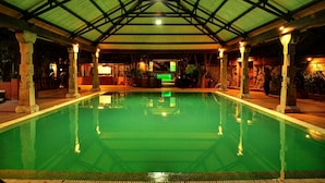 Piscina interna com teto alto e colunas, rodeada por área coberta com assentos e bar.