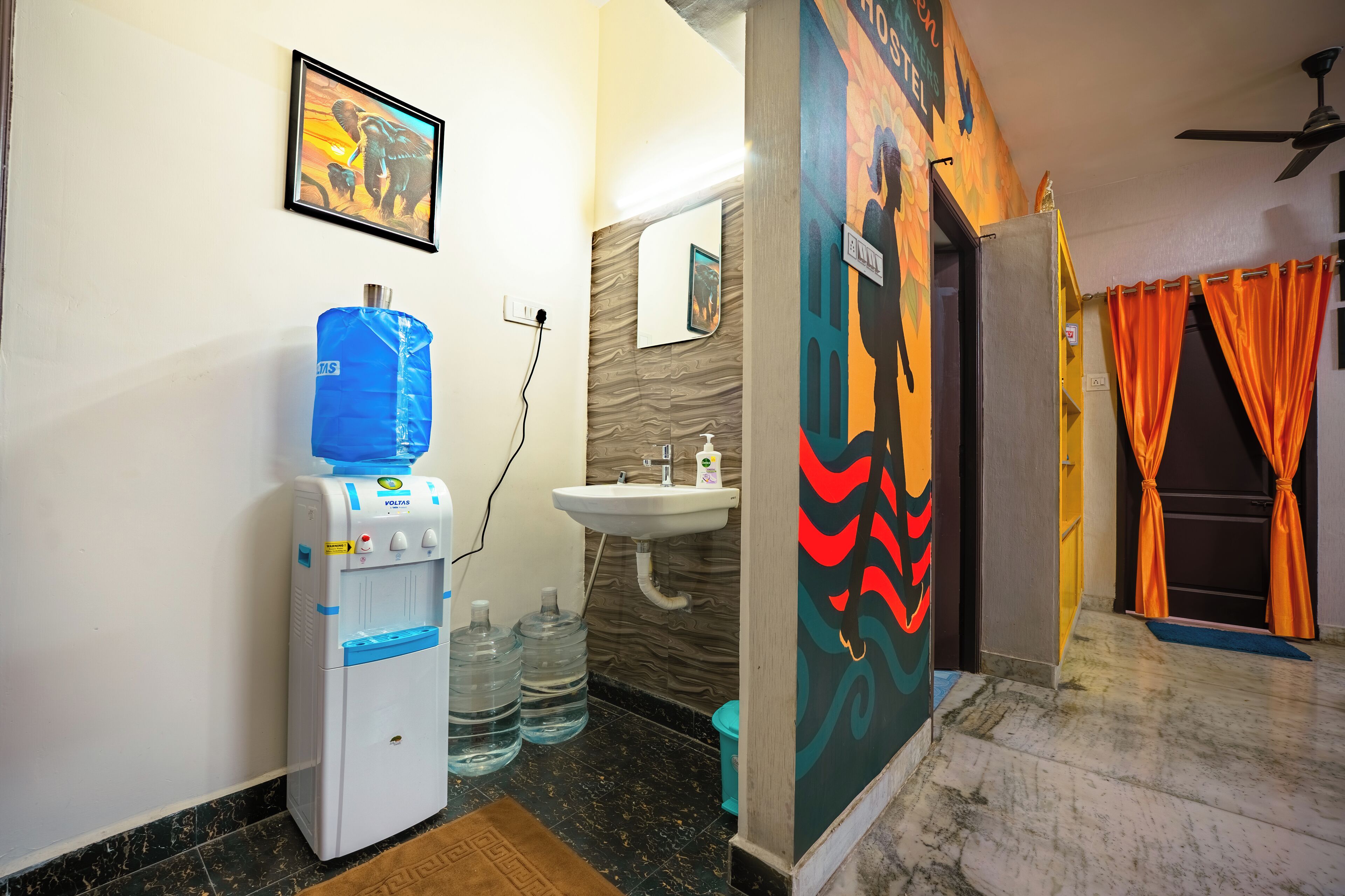 Casa de banho de hotel com dispensador de água, pia e grandes jarros de água.