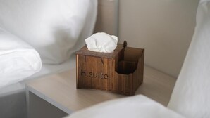 Caixa de lenços de madeira com a etiqueta 'H. suite' sobre uma mesa de cabeceira em quarto de hotel.
