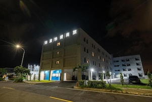 Um hotel com vários andares, sinalização iluminada, área de estacionamento e entrada bem iluminada.