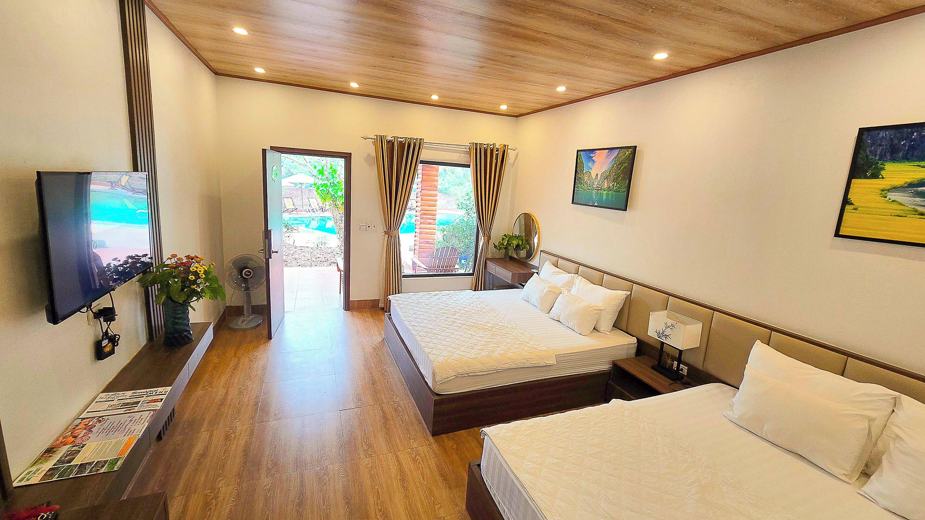 Quarto com cama, televisão, ventilador e janela com cortinas.