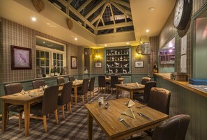 Restaurante com chão de ladrilhos xadrez, mesas e cadeiras de madeira.
