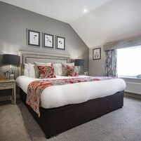 Quarto com cama grande, duas mesas de cabeceira com abajures, janela com cortinas e três quadros na parede.