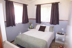 Quarto com cama, mesa de cabeceira, luminária e cortinas.