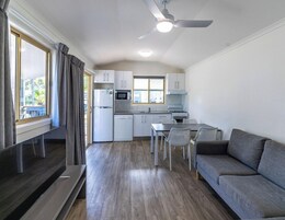Cozinha compacta com armários brancos, micro-ondas e fogão. Há uma área de refeições com mesa e cadeiras, e um sofá cinza.