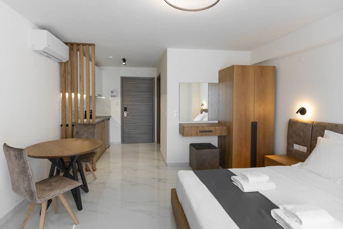 Quarto de hotel moderno com cama, mesa de cabeceira, divisória de madeira separando a área de dormir da área de jantar.