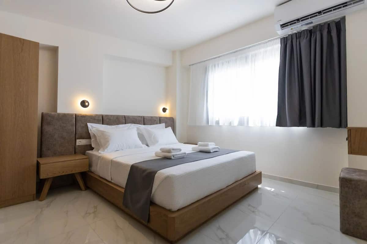 Quarto moderno com uma cama grande, mesas de cabeceira e janela com cortinas.