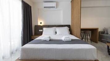 Quarto de hotel moderno com uma cama grande, mesa de cabeceira, uma poltrona e uma escrivaninha com cadeira.