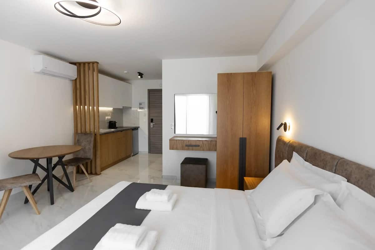 Quarto de hotel moderno com cama, mesa de cabeceira e pequena área de trabalho com cadeira.