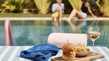 Ambiente à beira da piscina com mesa, servindo um hambúrguer, batatas fritas e um copo de vinho.