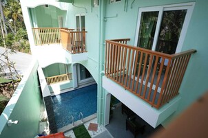 Um edifício de dois andares com piscina no andar térreo, grades de madeira nas varandas e vista para palmeiras.