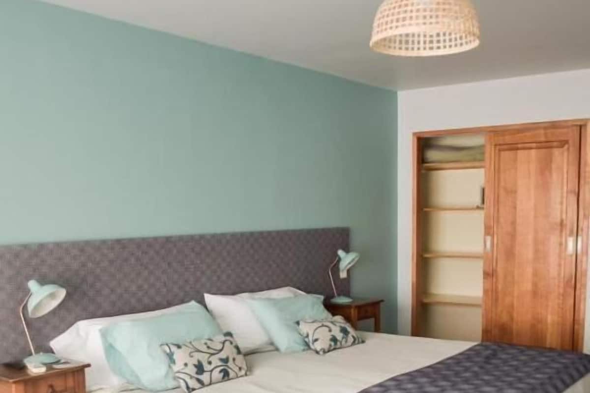 Quarto com cama, mesas de cabeceira, luminária, arandela e guarda-roupa.