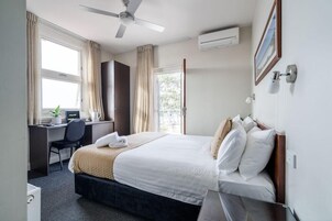 Quarto de hotel com cama, escrivaninha, cadeira e ventoinha no teto.