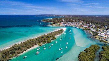 Vista aérea de uma área costeira com águas turquesa cristalinas, vários barcos e uma zona residencial com casas e vegetação.