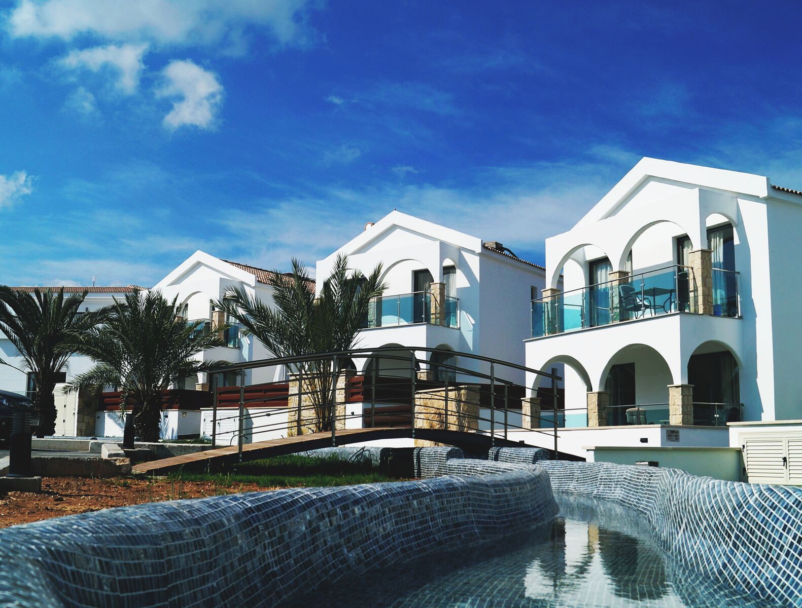 Um resort moderno com edifícios brancos, uma ponte e uma piscina.