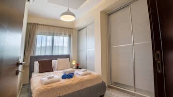 Quarto de hotel com cama, mesa de cabeceira, luminária, janela com cortinas e porta de correr.