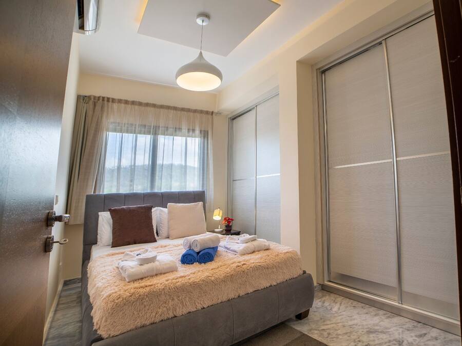 Quarto de hotel com cama, mesa de cabeceira, luminária, janela com cortinas e porta de correr.