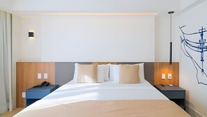 Quarto de hotel com uma cama grande, duas mesas de cabeceira, uma escrivaninha e uma obra de arte na parede.