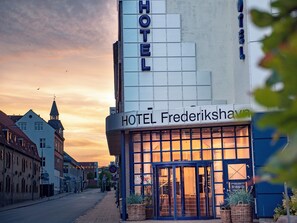 Entrada de hotel com uma placa indicando 'HOTEL Frederiksgaard' e vista da rua ao fundo.