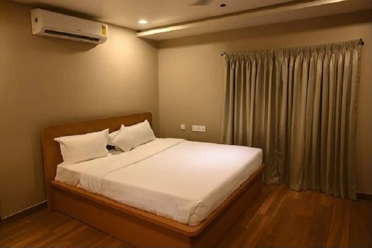 Cama bem arrumada em quarto com cabeceira de madeira, paredes bege e janela com cortinas.