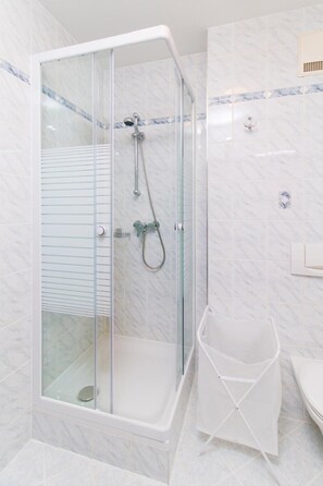 Casa de banho moderna com cabine de duche em vidro, lavatório branco e cadeira branca.