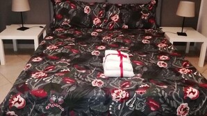 Quarto com colcha florida, um quadro emoldurado acima da cama e duas mesas de cabeceira com luminárias.