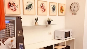 Uma cozinha compacta com máquina de café, micro-ondas e uma prateleira branca decorada.