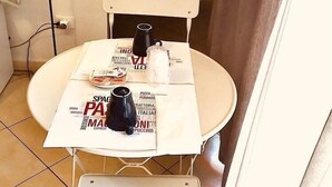 Uma pequena área de refeições com uma mesa redonda e duas cadeiras, uma revista, uma xícara de café preto e uma caneca branca.