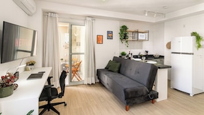 Um apartamento moderno com cozinha compacta, um sofá cinzento, área de jantar e televisão fixada na parede.