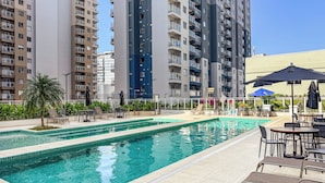 Uma piscina com espreguiçadeiras e guarda-sóis, cercada por edifícios residenciais altos.