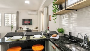 Cozinha moderna com televisão embutida exibindo 'NETFLIX', bancada de granito, banquetas de madeira e uma pia.
