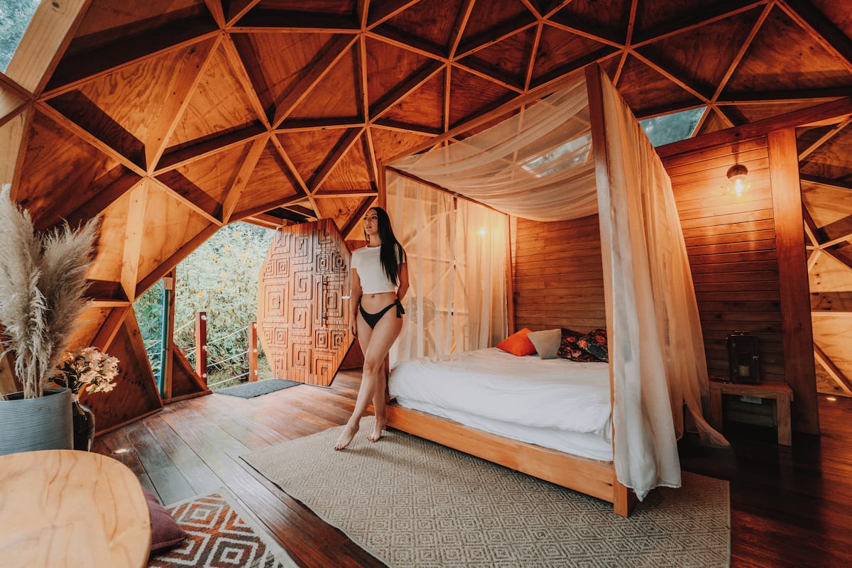 Uma cabana de madeira com uma cama, uma mesinha e um vaso de planta.