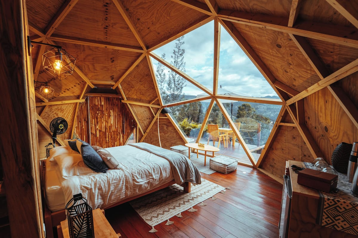 Um quarto aconchegante com uma cama grande, piso de madeira e vista por uma janela triangular.