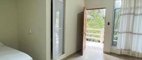 Quarto com cama, porta de correr para uma varanda e janela com cortinas.