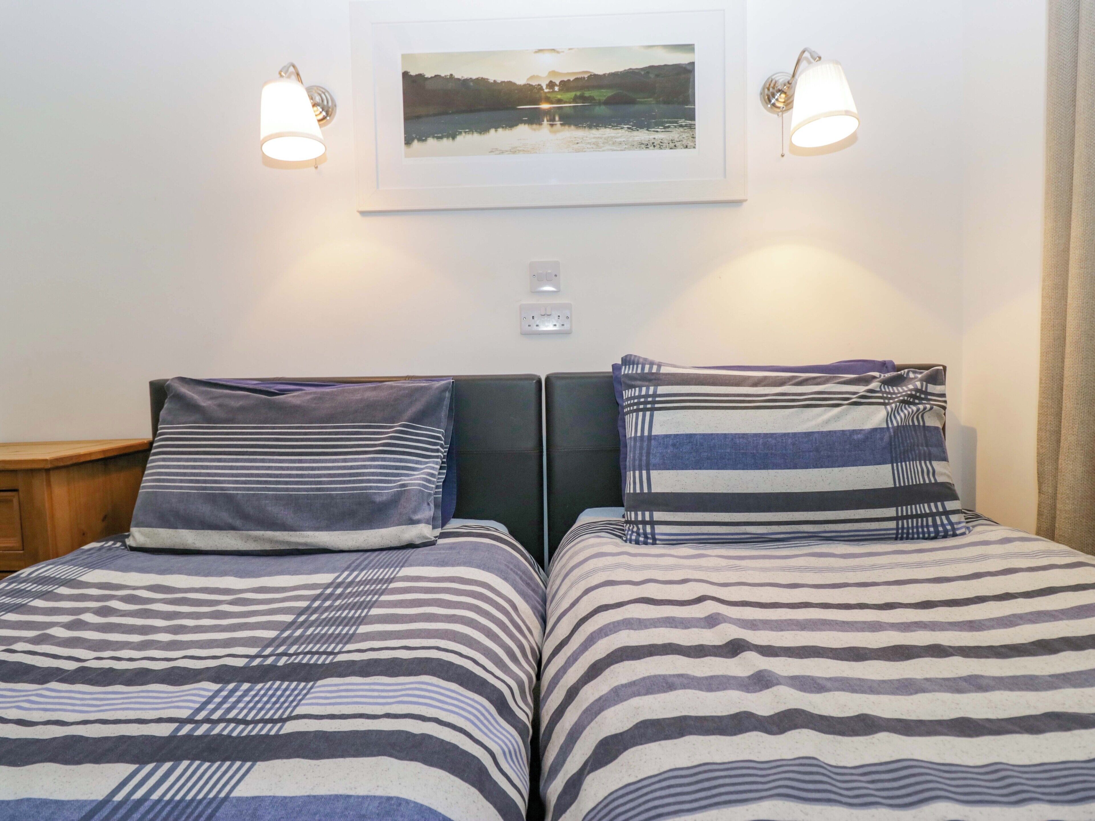 Uma cama de casal com roupa de cama listrada, duas luminárias fixadas na parede e um quadro acima da cama.