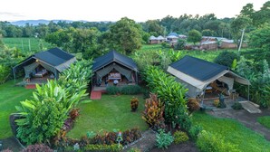 Um camping com três tendas, cada uma com varanda e área de estar, rodeado por vegetação exuberante e vista para colinas distantes.